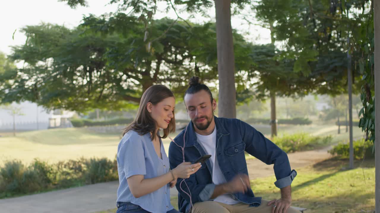 A young smiling couple sharing music with the same wired headphone at ...