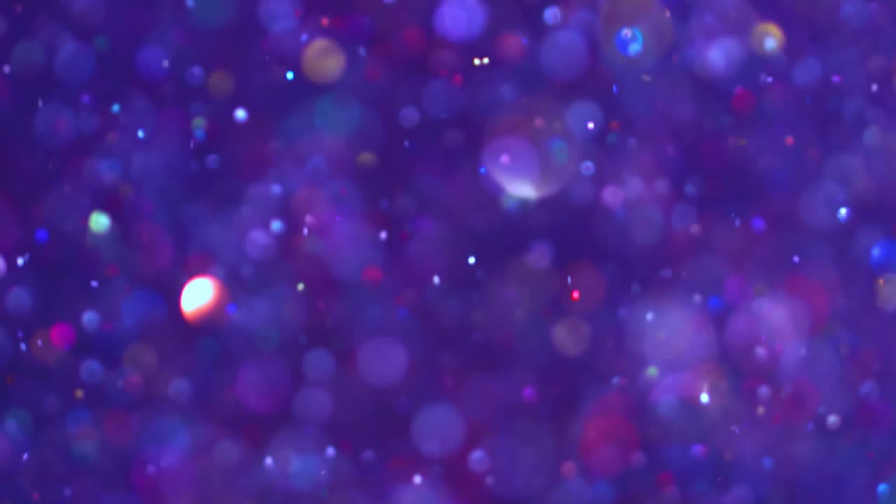 Close up shot of shimmering confetti falling over a purple background ...