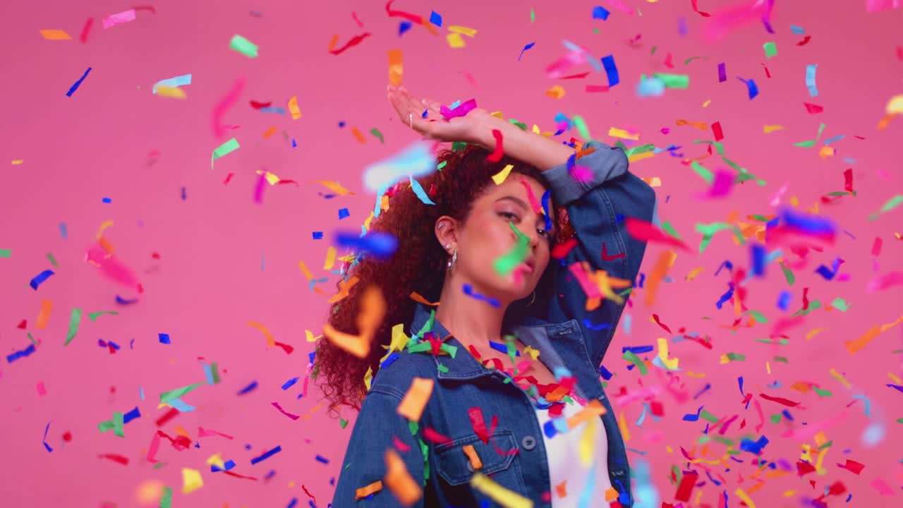 A young woman striking a pose while multicolored confetti flows upwards ...