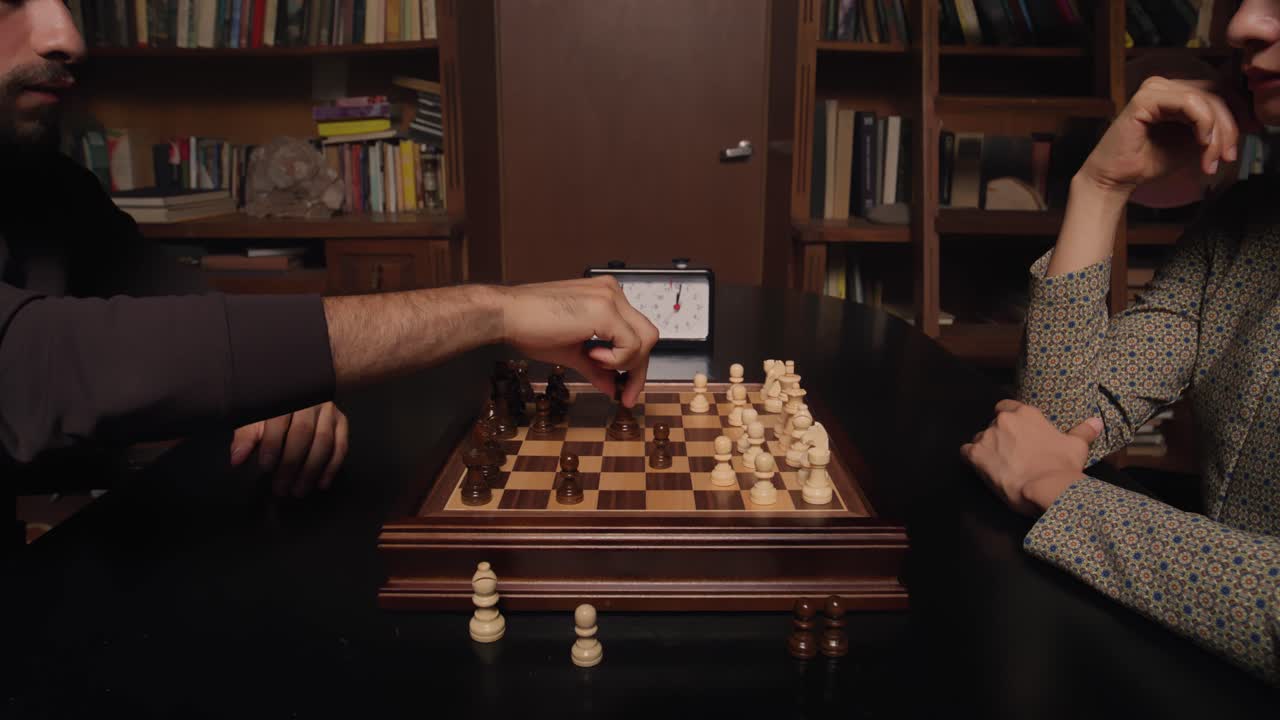 A young couple playing chess surrounded by bookshelves - Free Stock Video