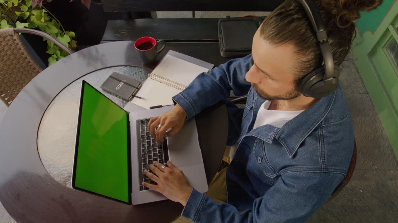 A man sitting on a cafe table types on his laptop computer showing a ...