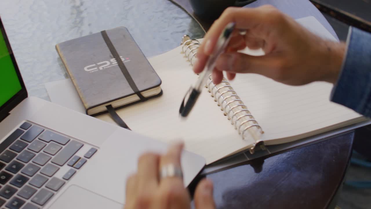 Beside a modern laptop the hands write a note on a yellow page notebook ...