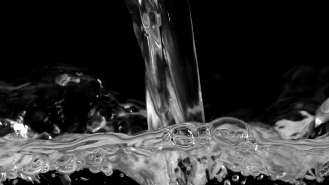 A stream of transparent water fills a container over a black background ...