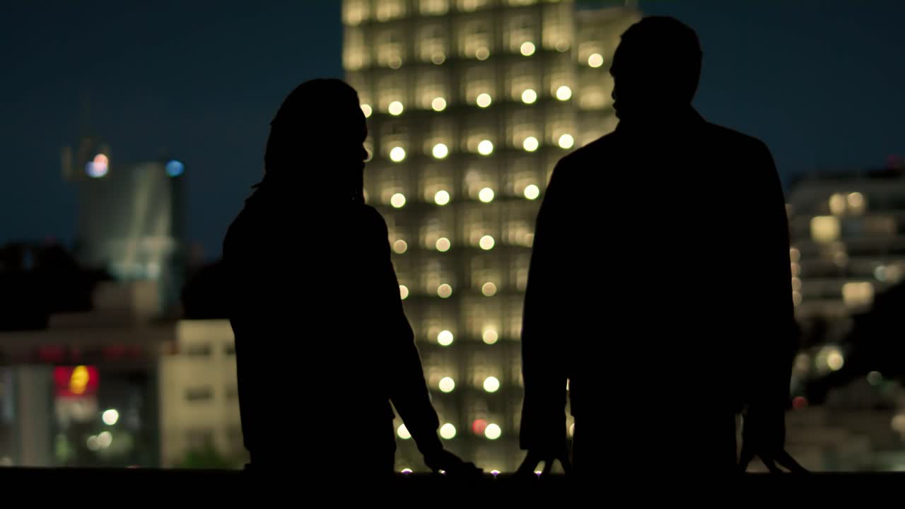 Silhouettes of Two People Against a Cityscape - Free Stock Video