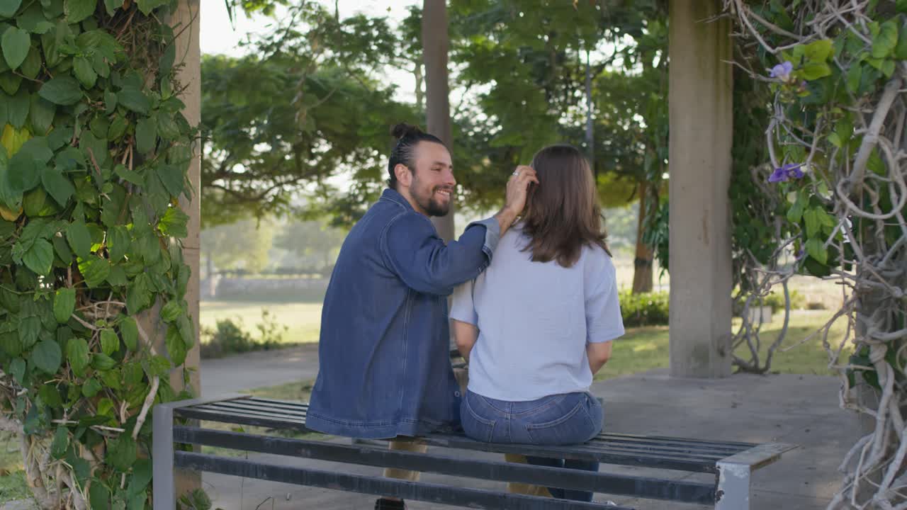 Sitting on a park bench a young man caresses the hair of her girlfriend ...