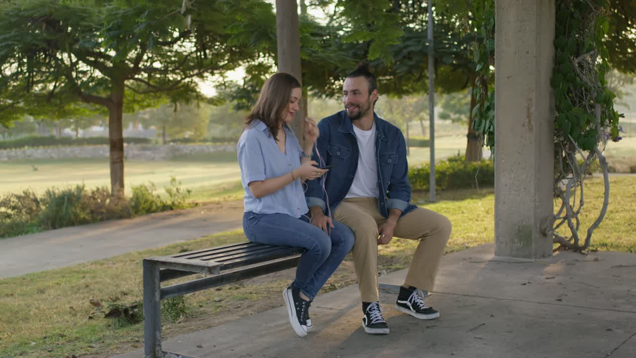 A young couple sharing music with a wired headphone sitting on a ...