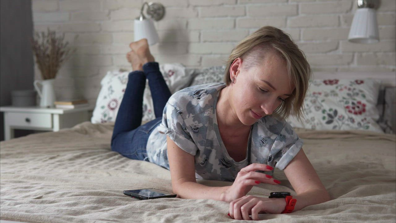 Laying on a bed checking her smartwatch - Free Stock Video