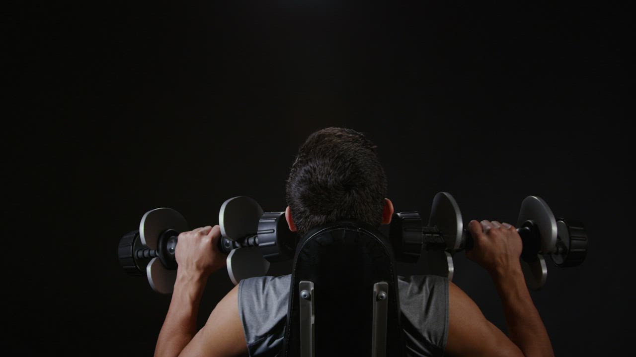 Lifting weights against a dark background - Free Stock Video
