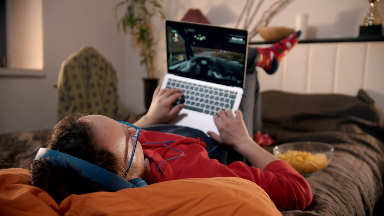 Young man lying on the bed playing video games on a laptop - Free Stock ...