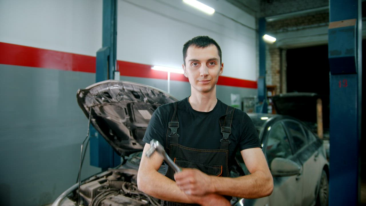 Mechanic holding a repair tool with a broken car in the background ...