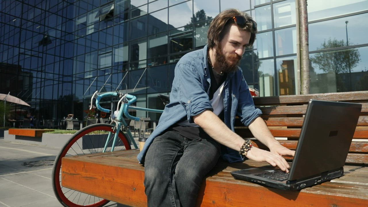 Man surfs internet on laptop from street bench - Free Stock Video