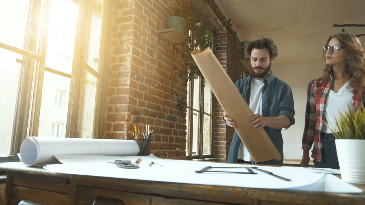 Designers unroll plans onto desk in studio - Free Stock Video