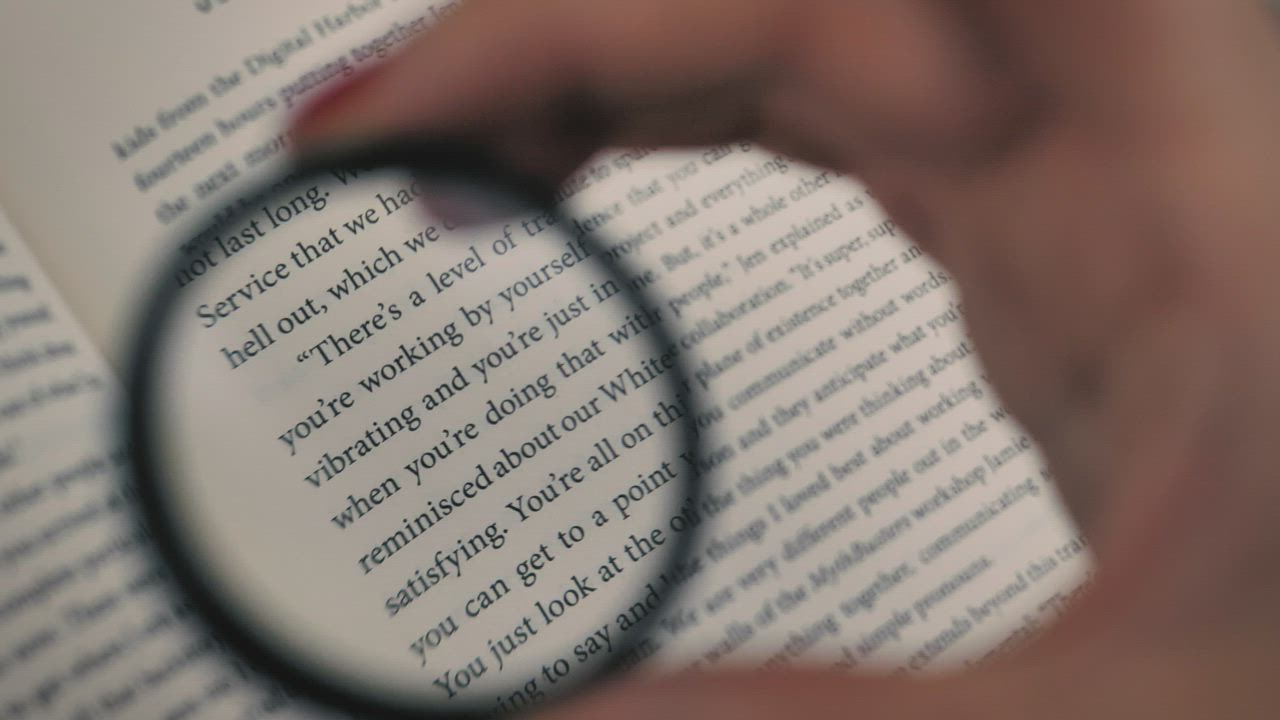 Hand of a person using a magnifying glass to read a book - Free Stock Video