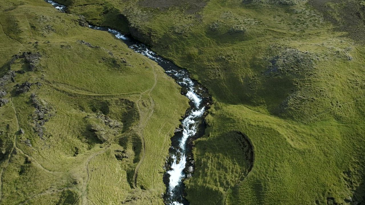 Aerial view of a river and a waterfall on a green land - Free Stock Video