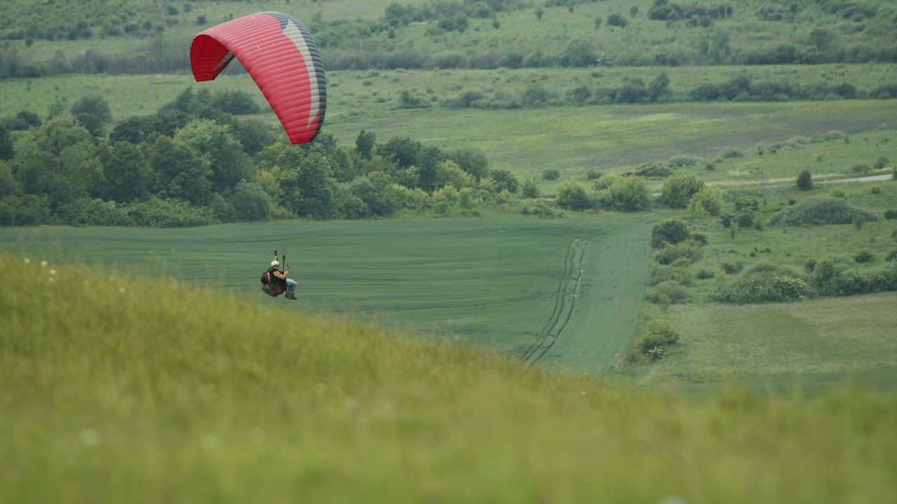 Paraglider floats over green countryside - Free Stock Video