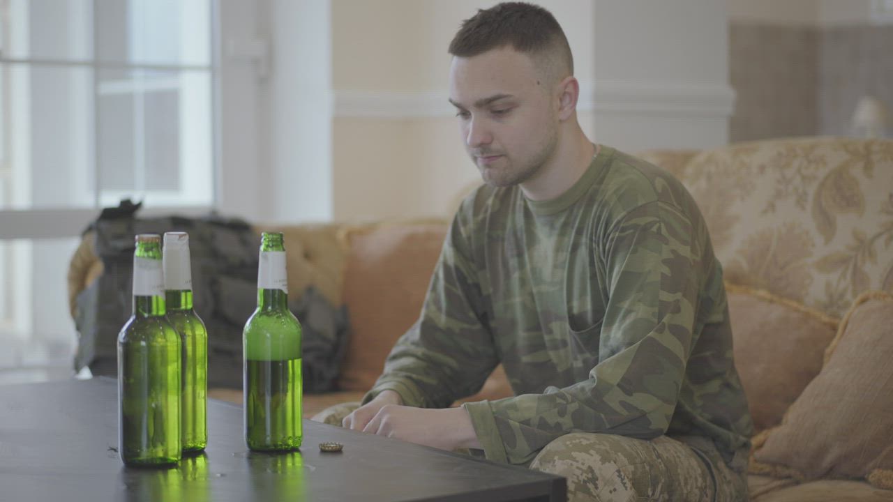 Upset Army veteran sits on sofa drinking beer - Free Stock Video