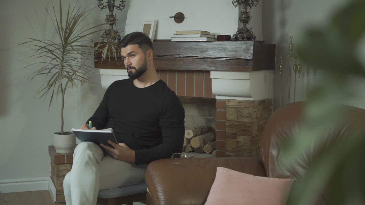 Man sits in living room thinking and writing - Free Stock Video