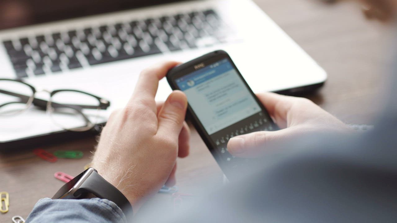 Hands scroll through Facebook on mobile at desk - Free Stock Video