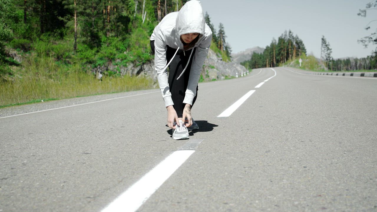 Runner ties laces before starting jog on mountain road - Free Stock Video