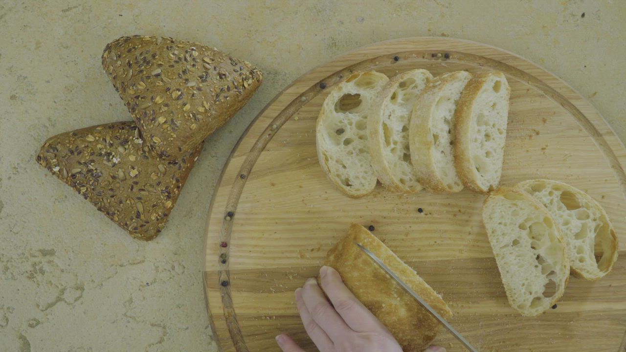 Top view of hands cutting fresh bread on wood board - Free Stock Video