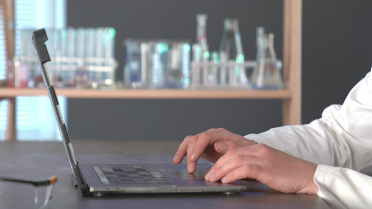 A Scientist typing on a laptop in the lab - Free Stock Video