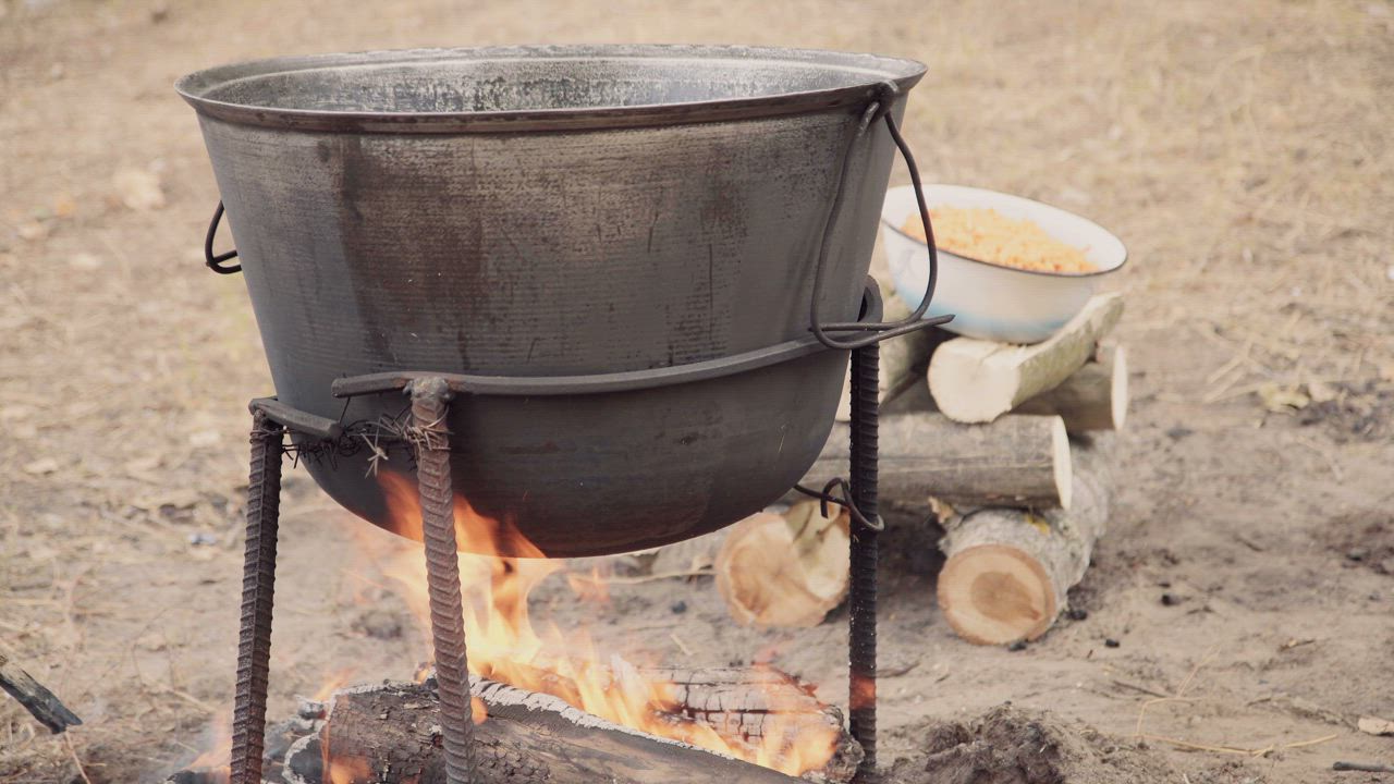 Cooking outdoors with a cauldron in the campfire - Free Stock Video