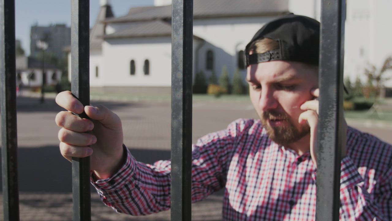 Man talking on the phone by a metal gate - Free Stock Video