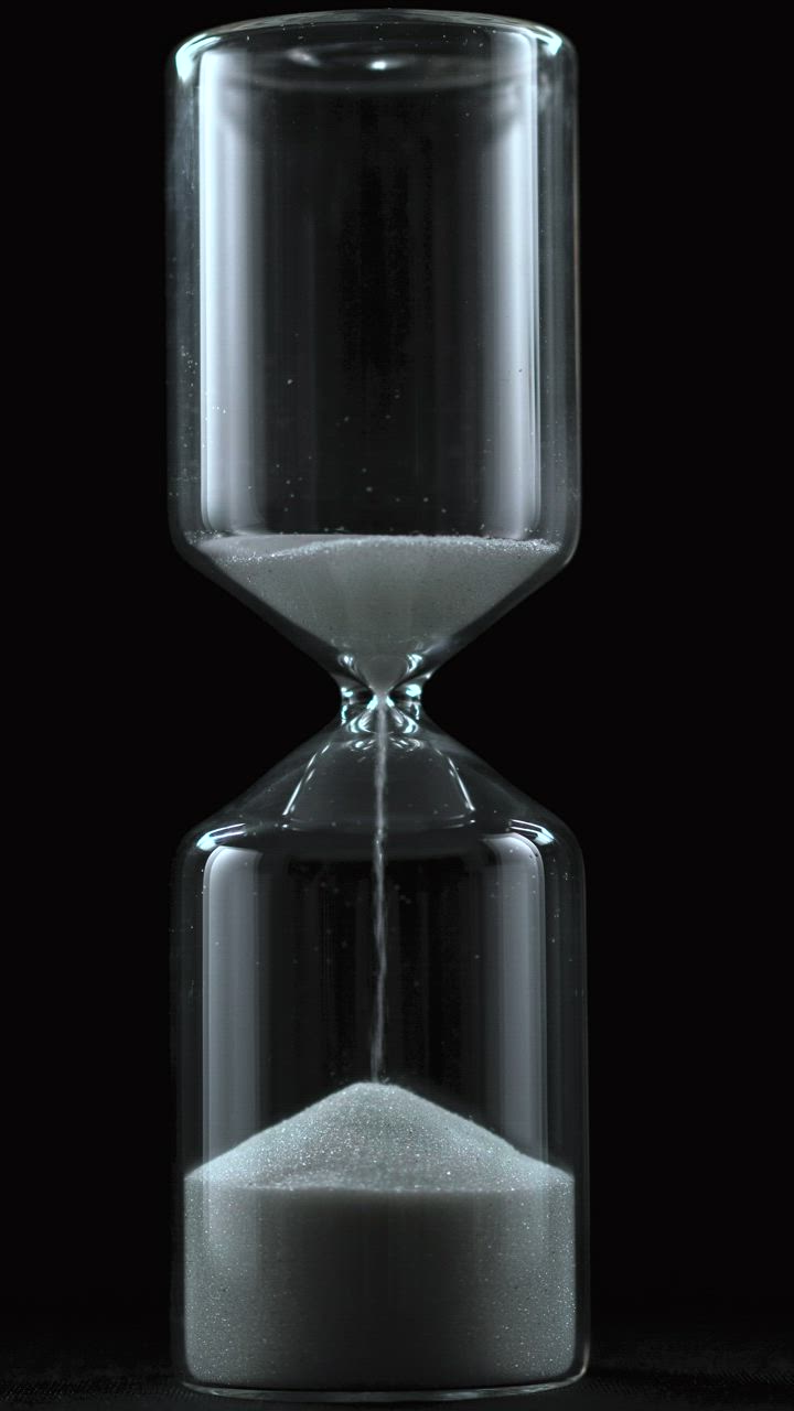 Sand falling from an hourglass on a black background - Free Stock Video