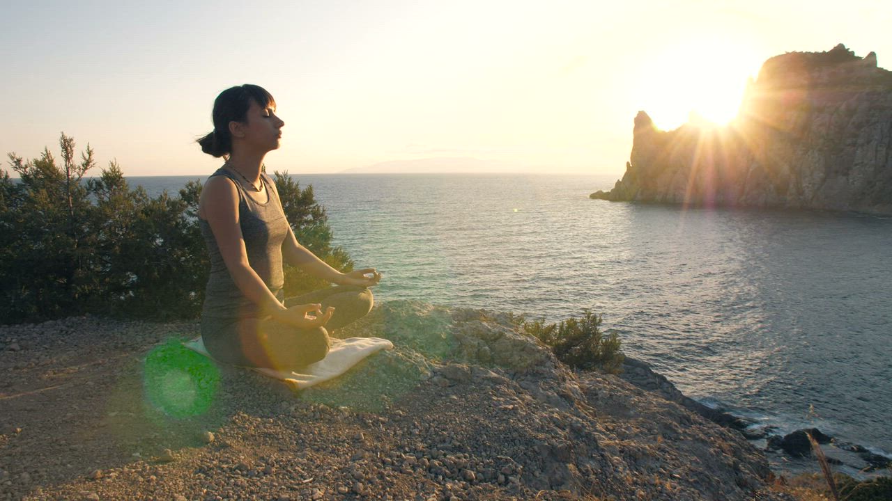 Woman meditating by the sea at sunset - Free Stock Video