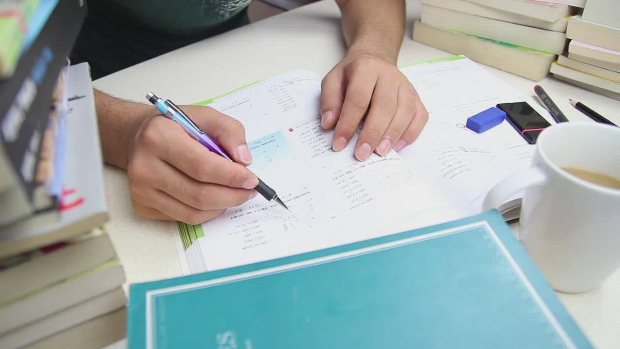 Student doing homework on a desk with many books - Free Stock Video