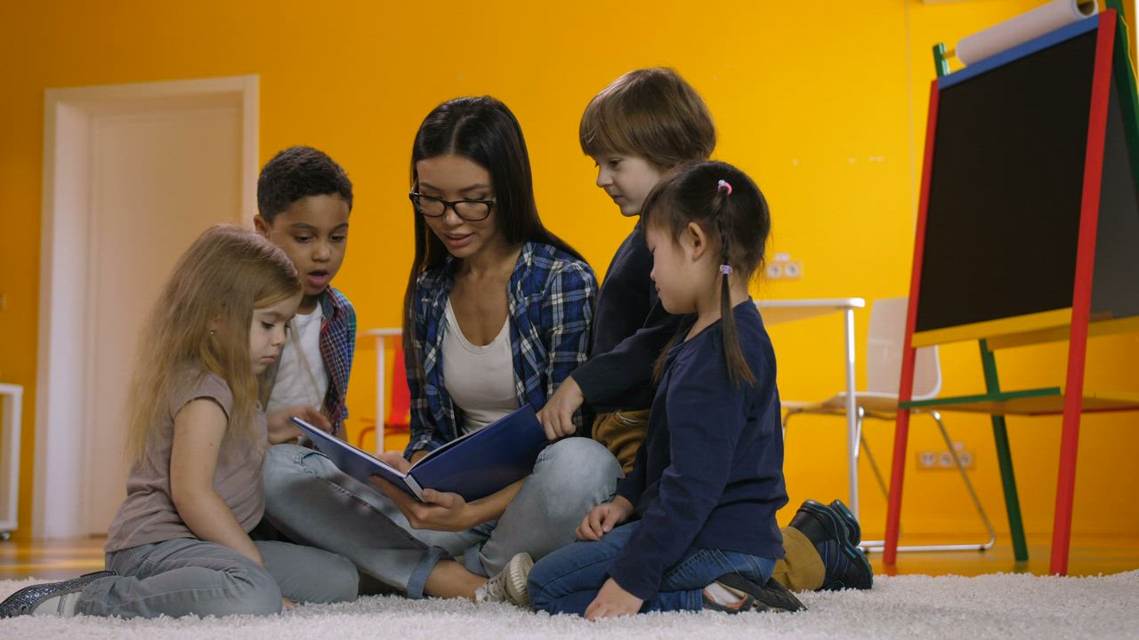 Teacher with some children reading a book together - Free Stock Video