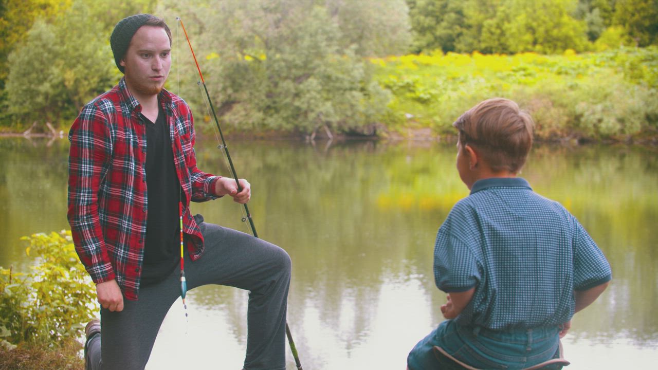 Young man gives a fishing rod to a boy in a lake - Free Stock Video