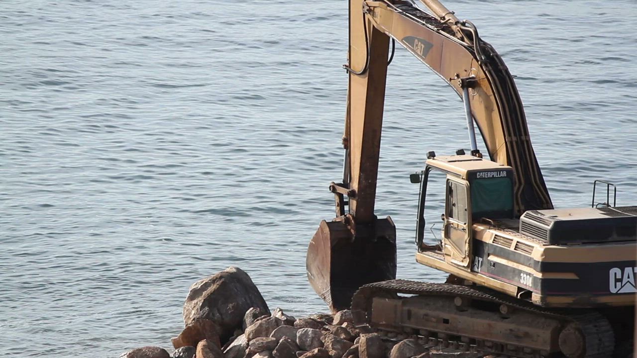 Crane digging on rocks at the sea - Free Stock Video