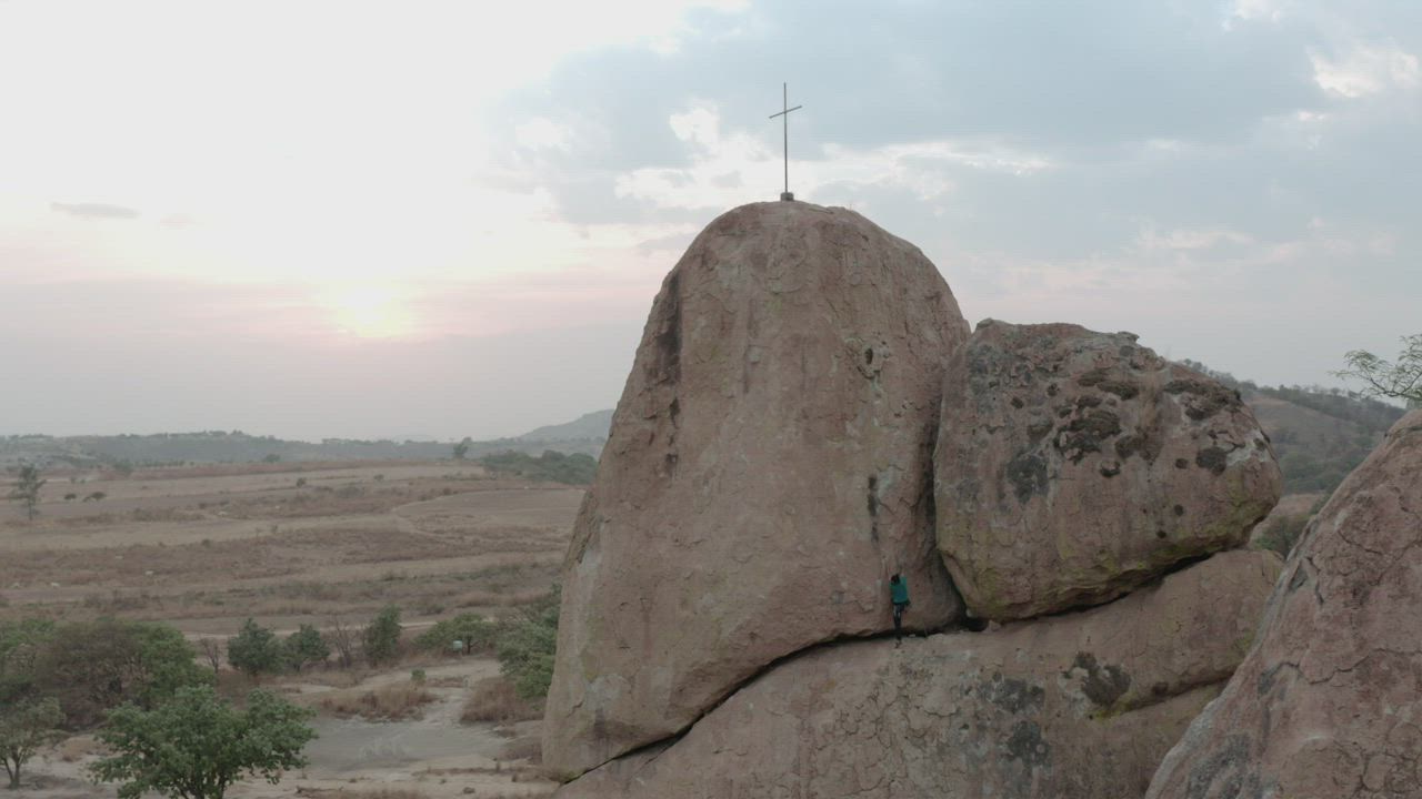 A young man is climbing a huge rock adorned with a religious cross at ...