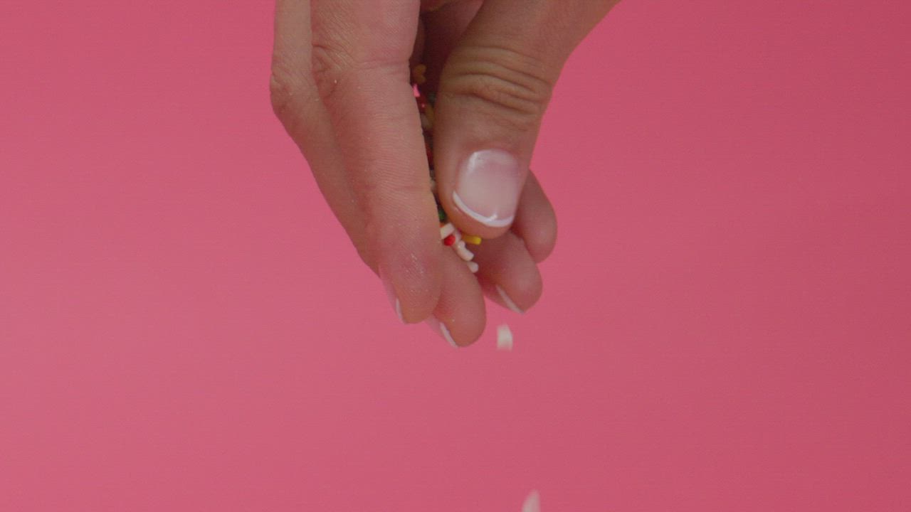 Woman sprinkling colored sprinkles on a donut - Free Stock Video