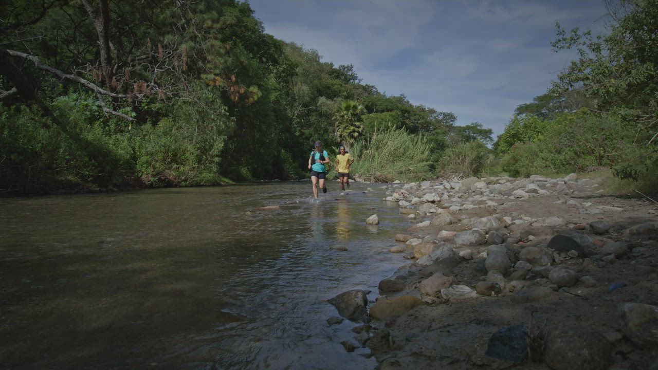 Woman and man jogging through the water of a river - Free Stock Video