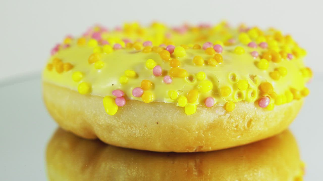 Rotating donut with yellow icing and sprinkles - Free Stock Video