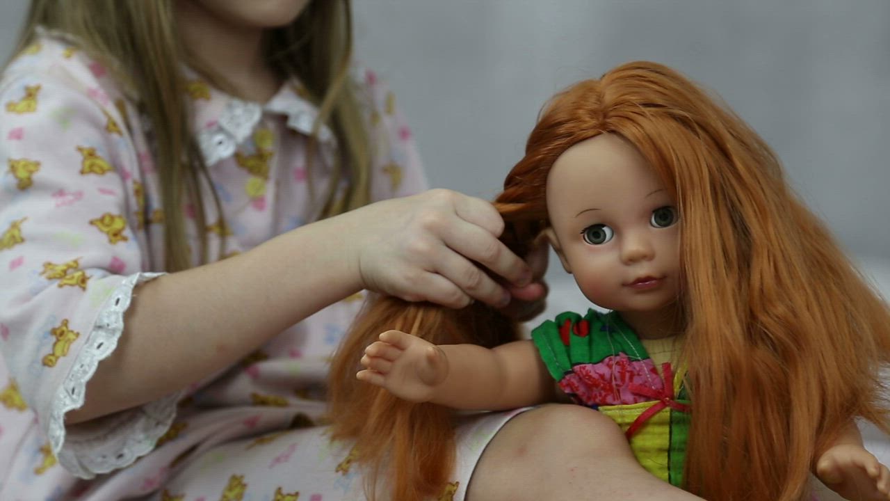 Child braids the hair of her doll - Free Stock Video