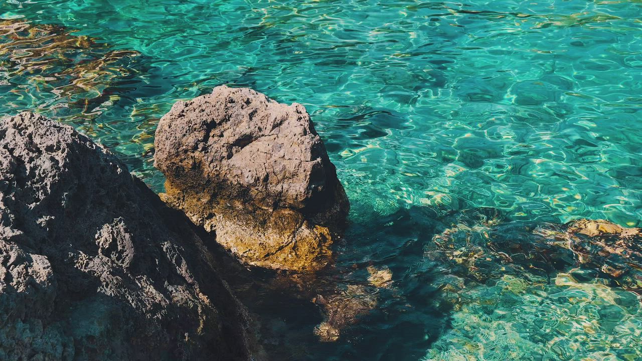 Crystal blue water around rocks in the sea - Free Stock Video