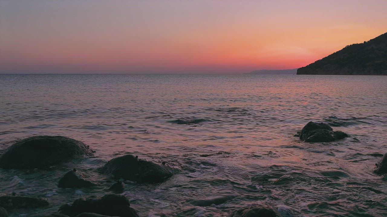 Waves breaking over rocks as the sun sets - Free Stock Video