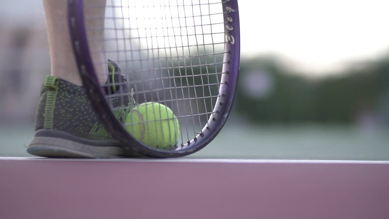 Tennis player holds tennis ball against foot with racket - Free Stock Video