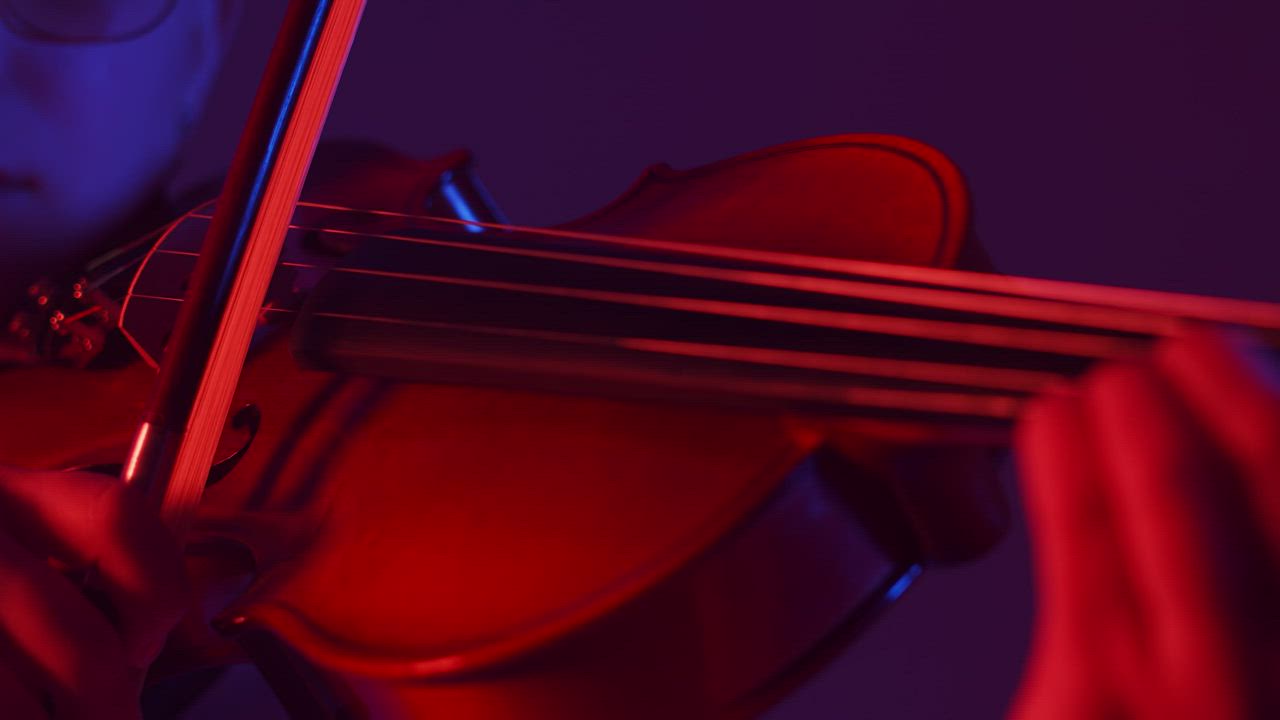 Close up of a violinist expertly playing a violin against a red light ...