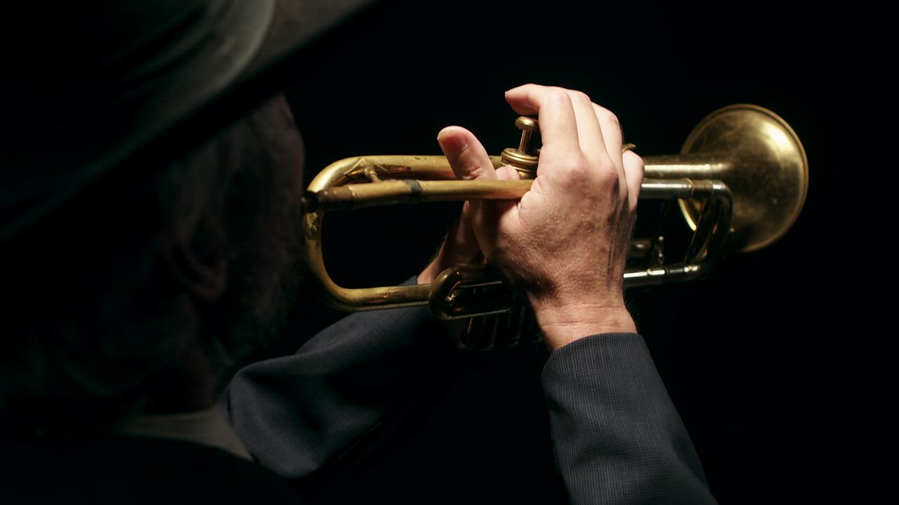 Musician playing a trumpet against a black backdrop - Free Stock Video