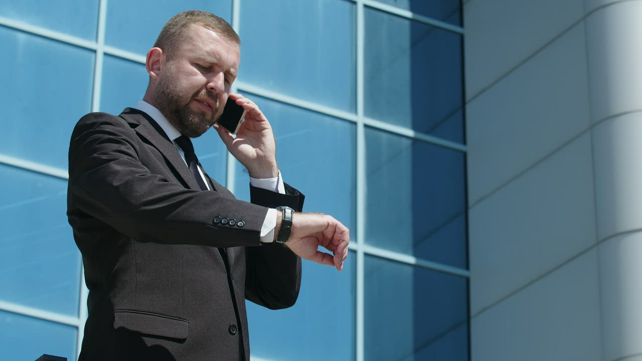 Businessman checking his watch while on a phone call - Free Stock Video