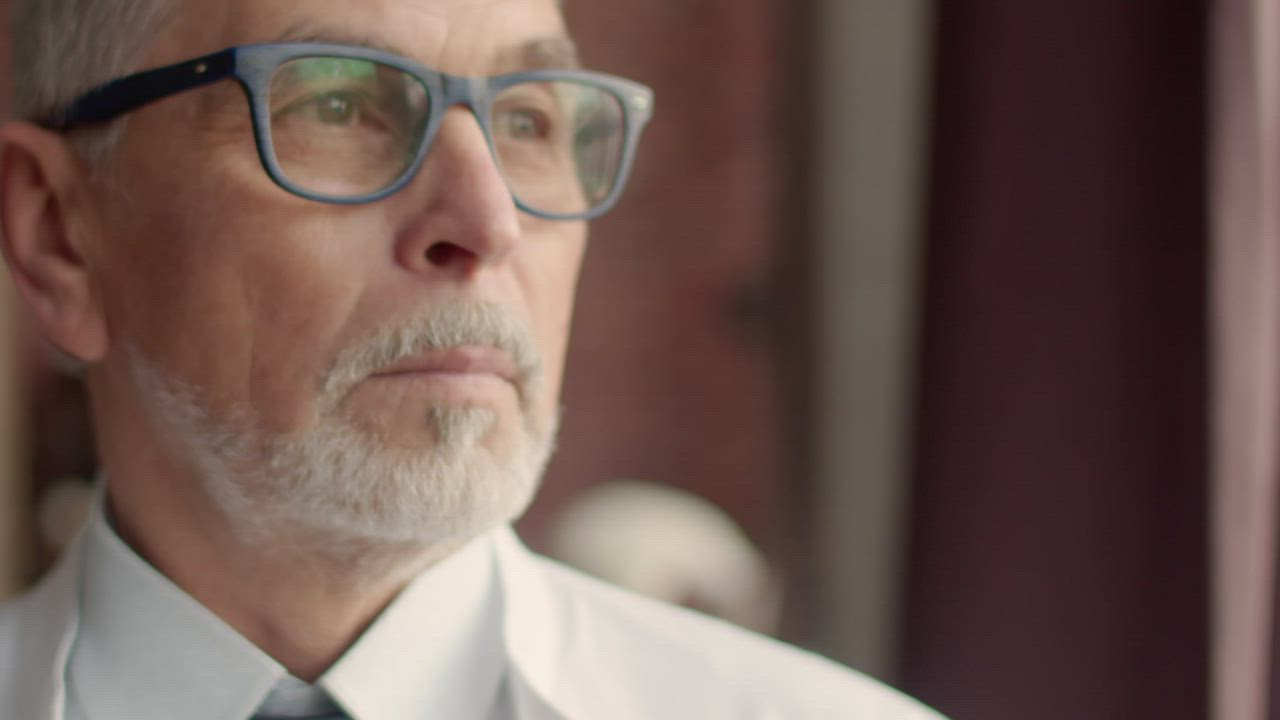 Doctor wearing glasses staring intensely out a window - Free Stock Video