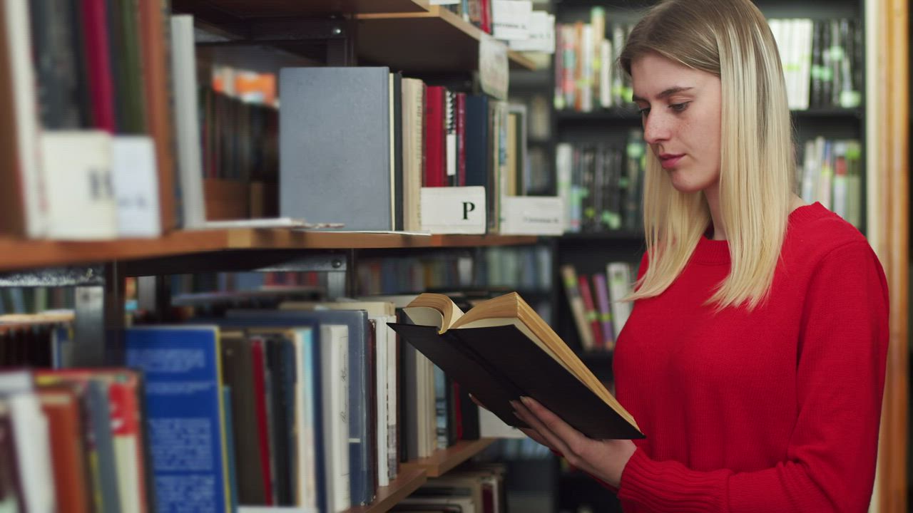 Student reading the pages of a book in a library - Free Stock Video