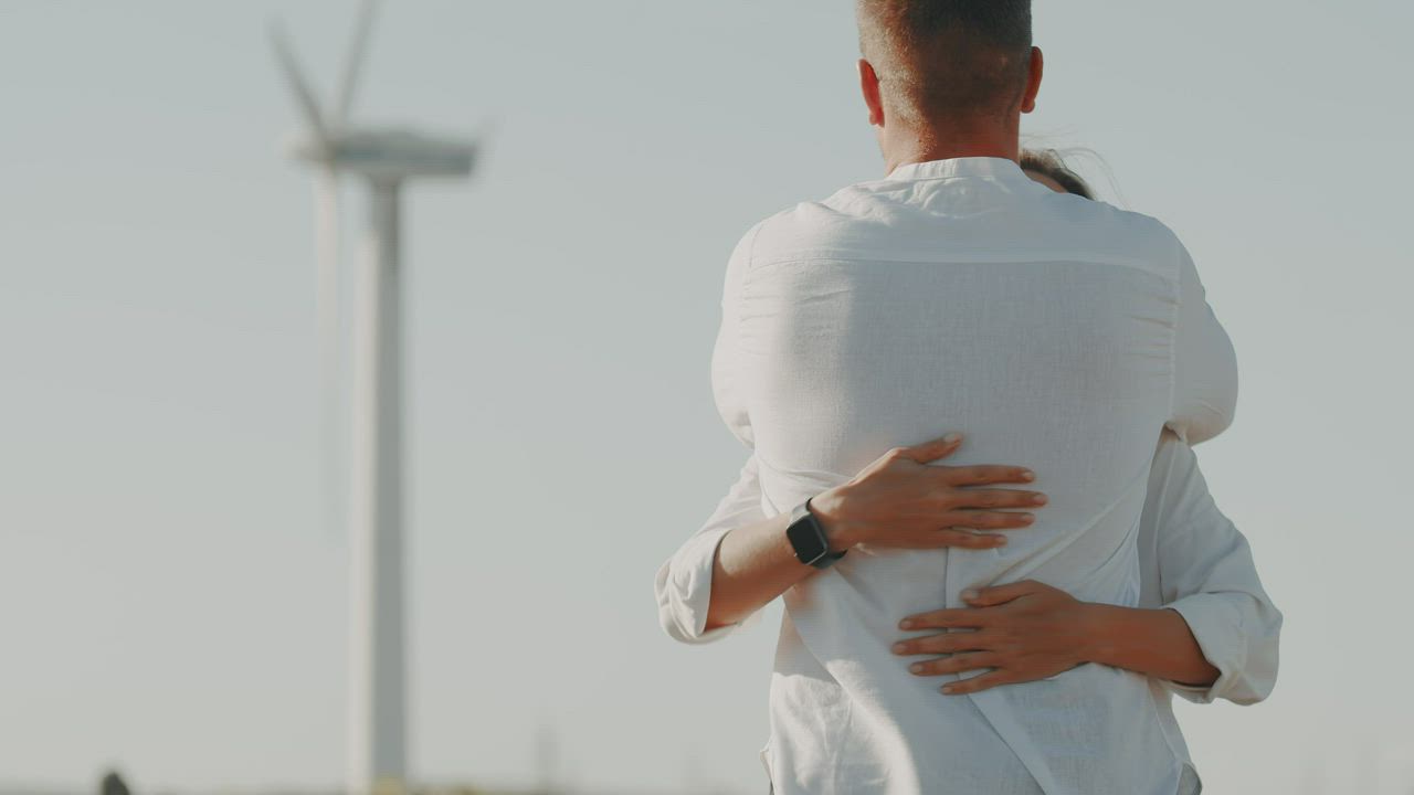 Couple embracing in the sunshine near a wind turbine - Free Stock Video