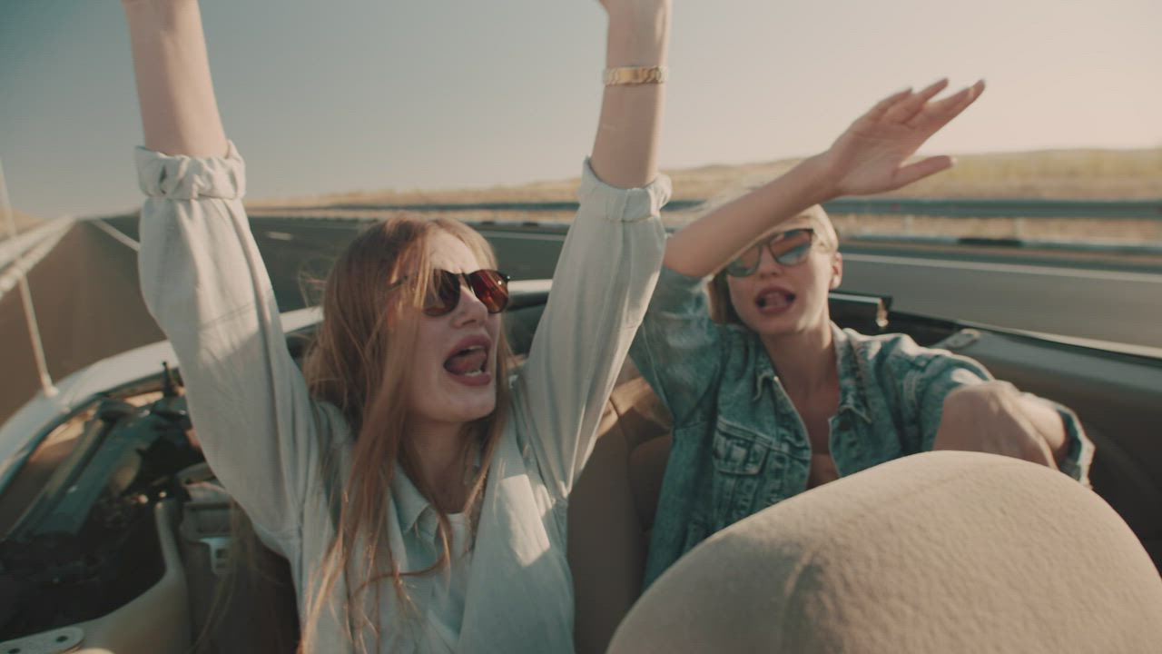 Friends having fun in the back of a convertible car on a roadtrip ...