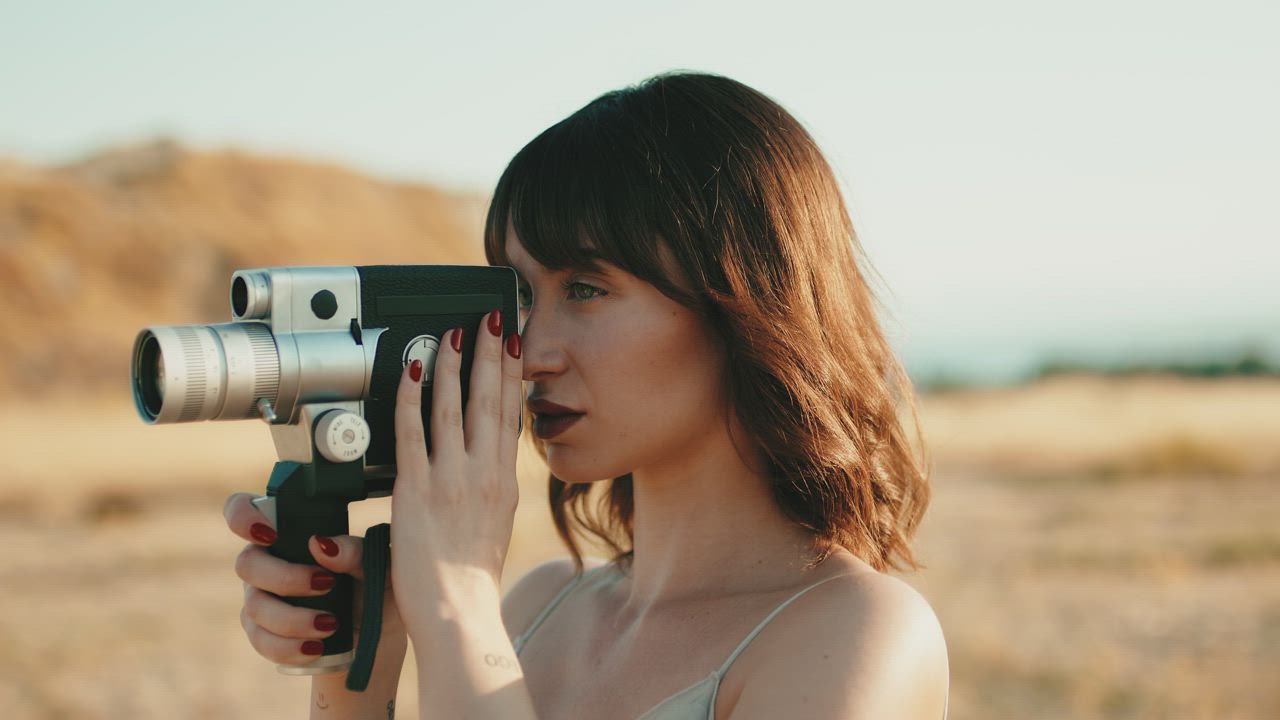 Side view of a woman filming with vintage 8mm camera in the countryside ...
