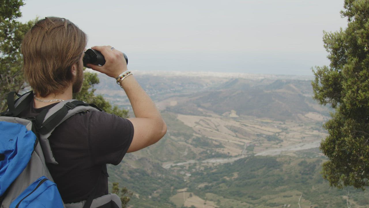 Man looking across a scenic landscape with binoculars - Free Stock Video